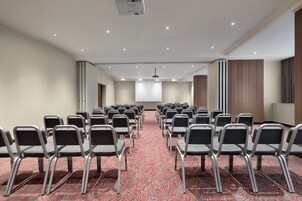 Uma sala de conferências com fileiras de cadeiras, uma tela de projetor e piso coberto de carpete.