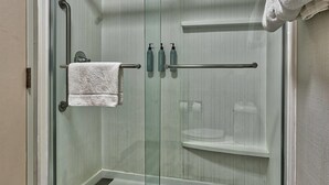 Um chuveiro com paredes de vidro, um porta-toalhas, uma porta de vidro e um prateleira com artigos de higiene pessoal.