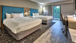 Quarto de hotel com duas camas, uma escrivaninha, uma cadeira, televisão e varanda com vista.