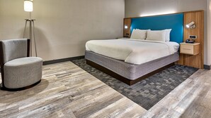 Quarto de hotel com cama, uma cadeira, luminária de chão e mesa de cabeceira.