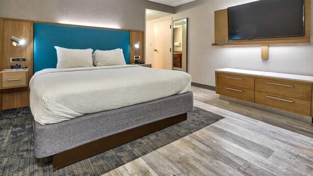 Quarto de hotel moderno com uma cama grande, uma televisão na parede e uma cômoda de madeira.
