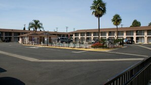 Um motel com estacionamento, uma área cercada com uma palmeira e um edifício com várias janelas.