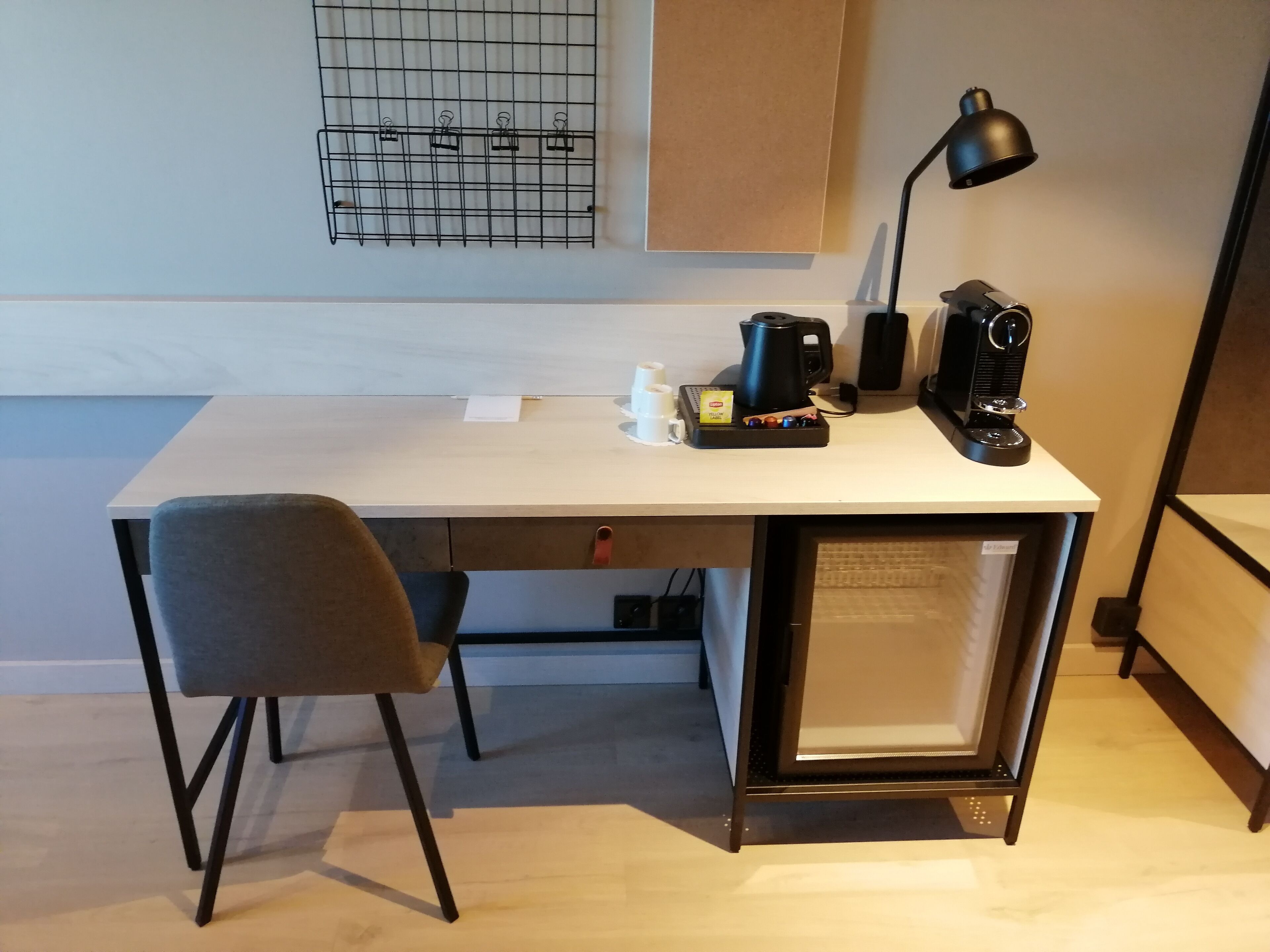 Um espaço de trabalho moderno com uma mesa branca, uma luminária preta, uma máquina de café e uma cadeira.