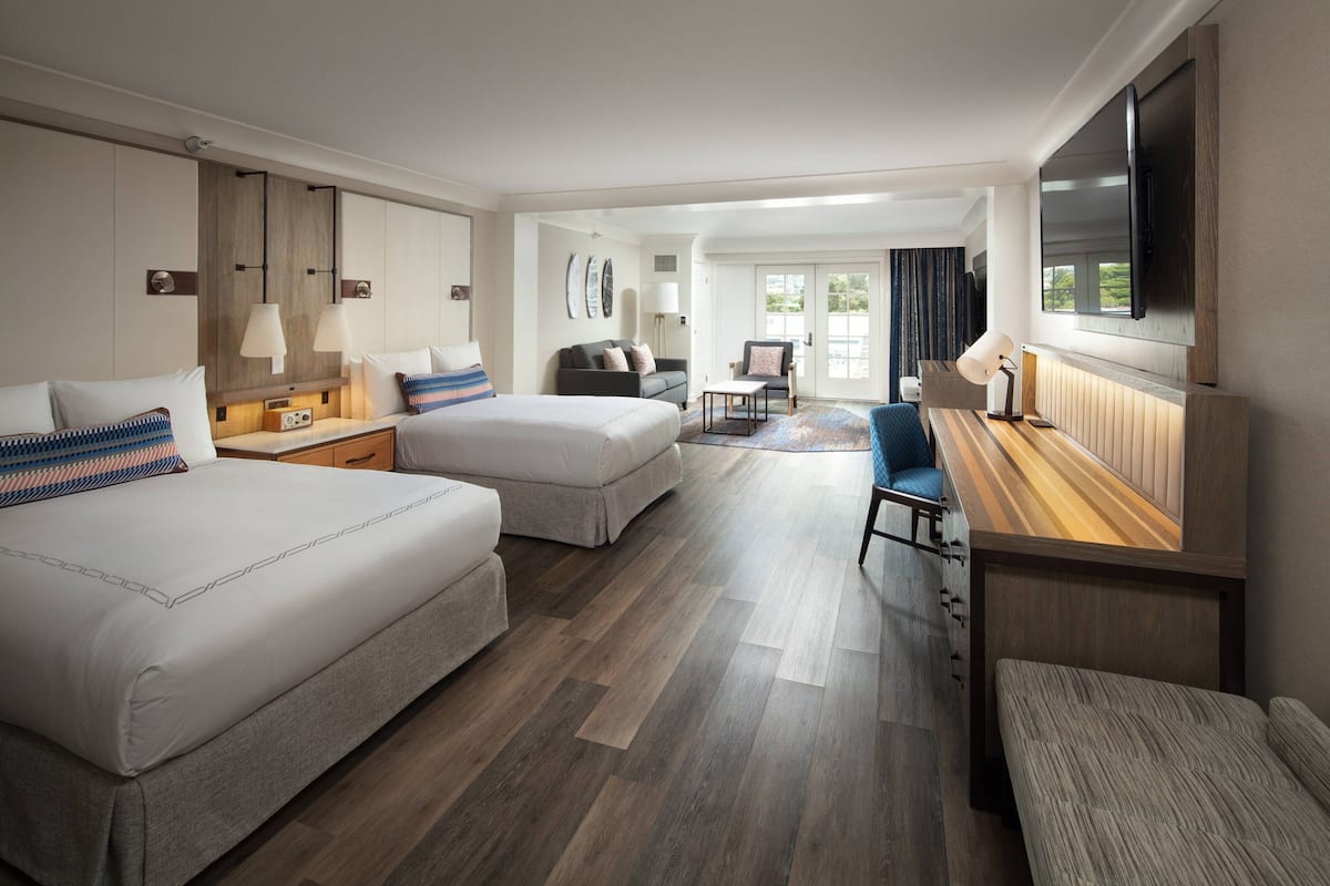 Quarto de hotel com duas camas, uma escrivaninha, televisão e vista para o exterior.