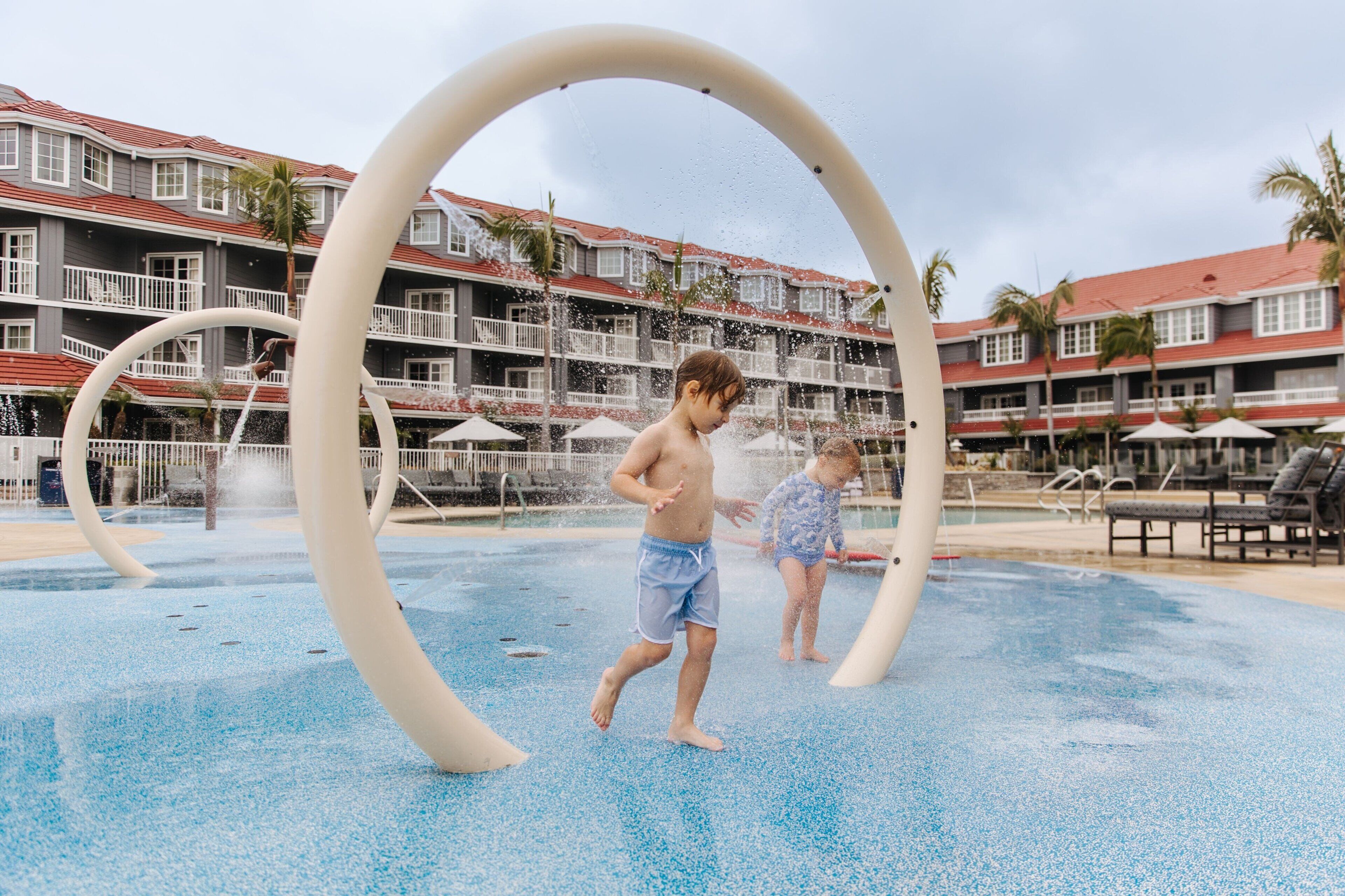 Área de piscina com elementos aquáticos e um hotel ao fundo.