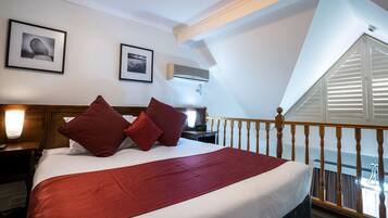 Quarto de hotel com uma cama grande, duas almofadas, uma mesa de cabeceira com abajur e duas imagens emolduradas na parede.