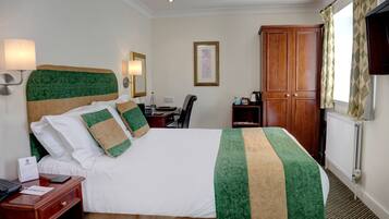 Quarto de hotel com uma cama grande, um guarda-roupa de madeira, uma escrivaninha com luminária e uma cadeira.