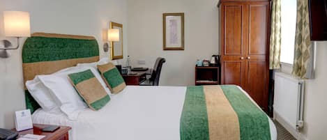 Quarto de hotel com uma cama grande, um guarda-roupa de madeira, uma escrivaninha com luminária e uma cadeira.