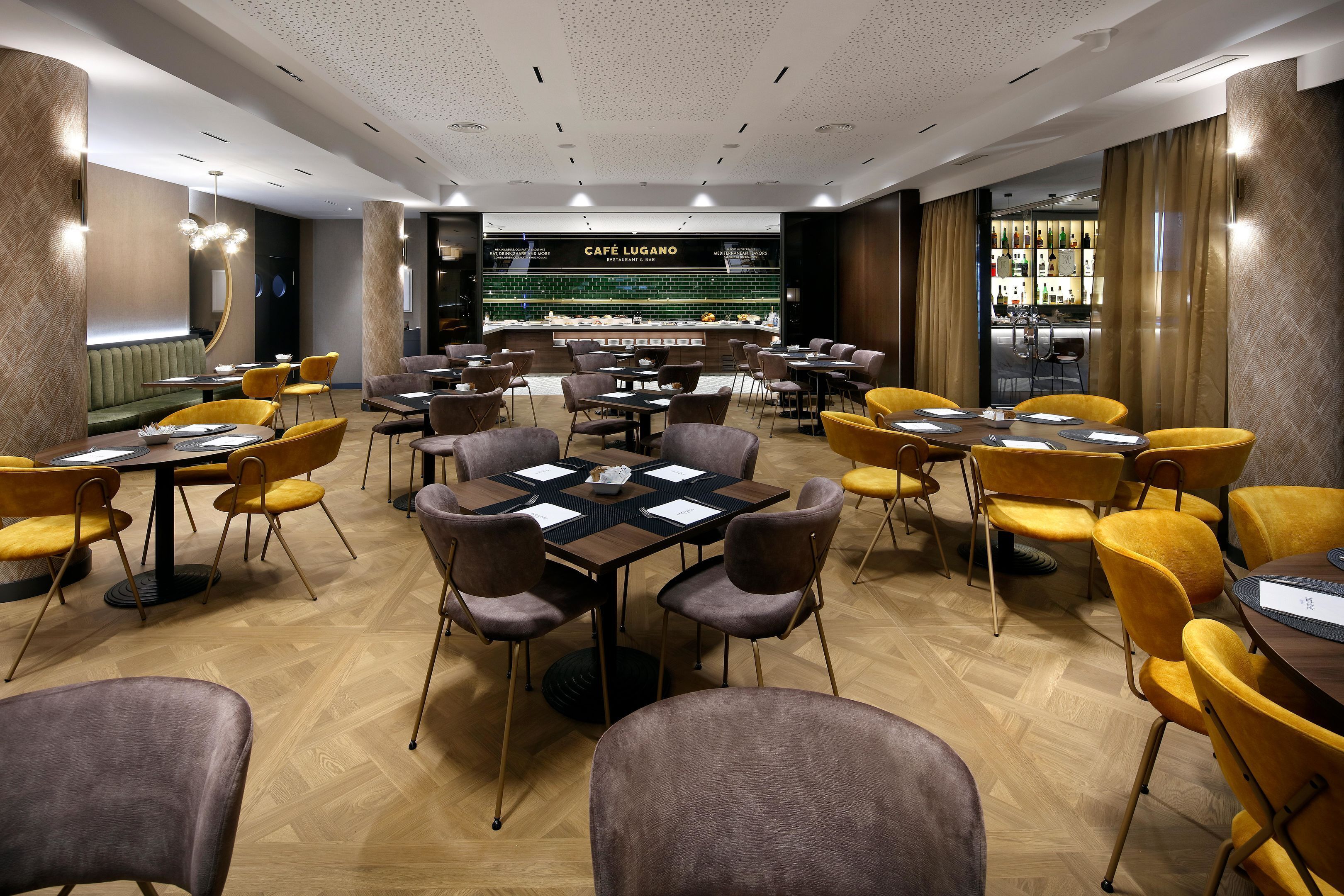 Um restaurante moderno com diversas áreas de refeição, incluindo mesas redondas e cabines, e um bar ao fundo.