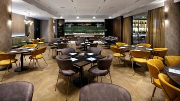 Um restaurante moderno com diversas áreas de refeição, incluindo mesas redondas e cabines, e um bar ao fundo.