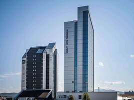 Um hotel moderno com fachada de vidro marcante e um edifício adjacente mais baixo com painéis solares no telhado.