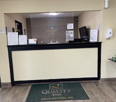 Balcão de recepção de hotel com uma placa indicando "Quality Inn" e um letreiro com a frase "We Care" acima.