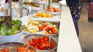 Uma área de buffet com diversas opções de comida, incluindo frutas, legumes e saladas.