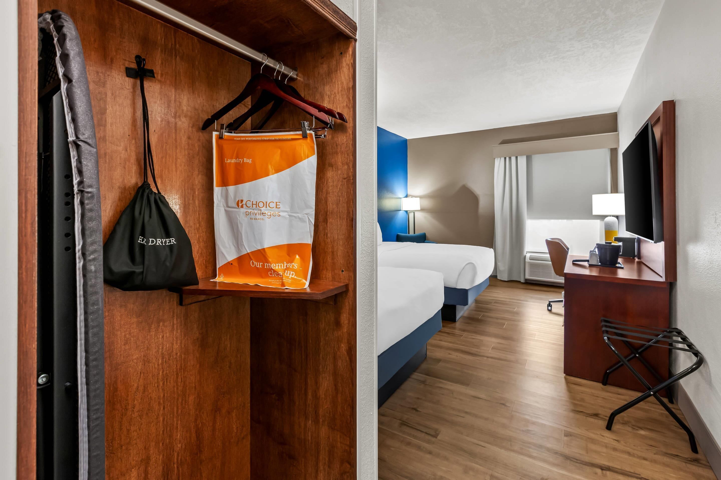 Quarto de hotel com guarda-roupa de madeira, cama, escrivaninha e televisão.