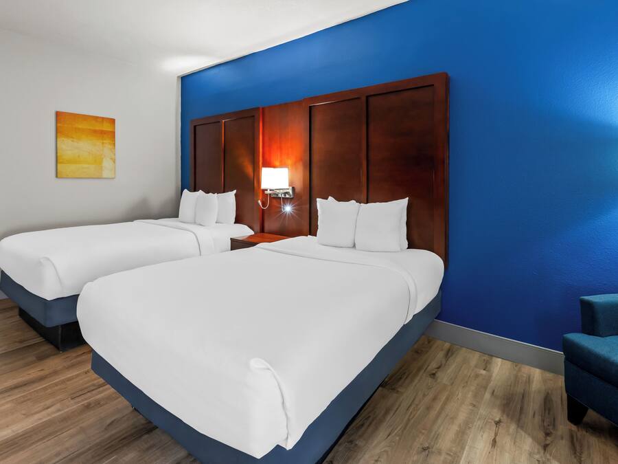 Quarto de hotel com duas camas, uma parede azul decorativa, um painel de cabeceira em madeira e uma mesa de cabeceira com abajur.