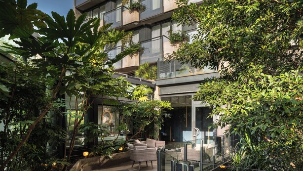 Um edifício moderno com varanda de vidro, vegetação exuberante e área de estar ao ar livre.