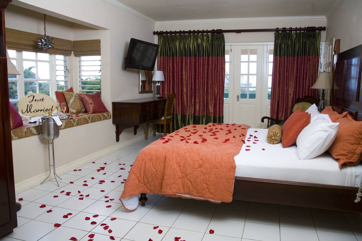 Um quarto com cama, escrivaninha, televisão e janela com cortinas.