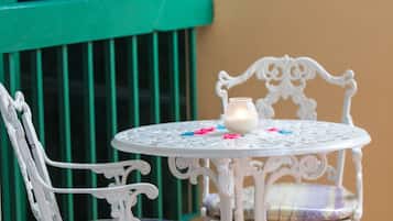 Conjunto de mesa e cadeira de metal branco numa varanda com guarda-corrimão verde.
