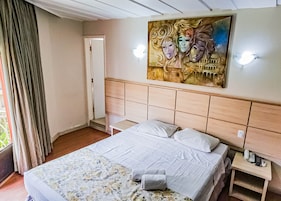 Quarto de hotel com cama, mesa de cabeceira, um quadro e vista para o exterior.