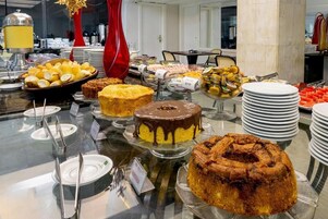Um buffet com diversos bolos e doces, incluindo um bolo de chocolate com efeito escorrendo, um bolo bundt e outro bolo bundt com um anel em cima.