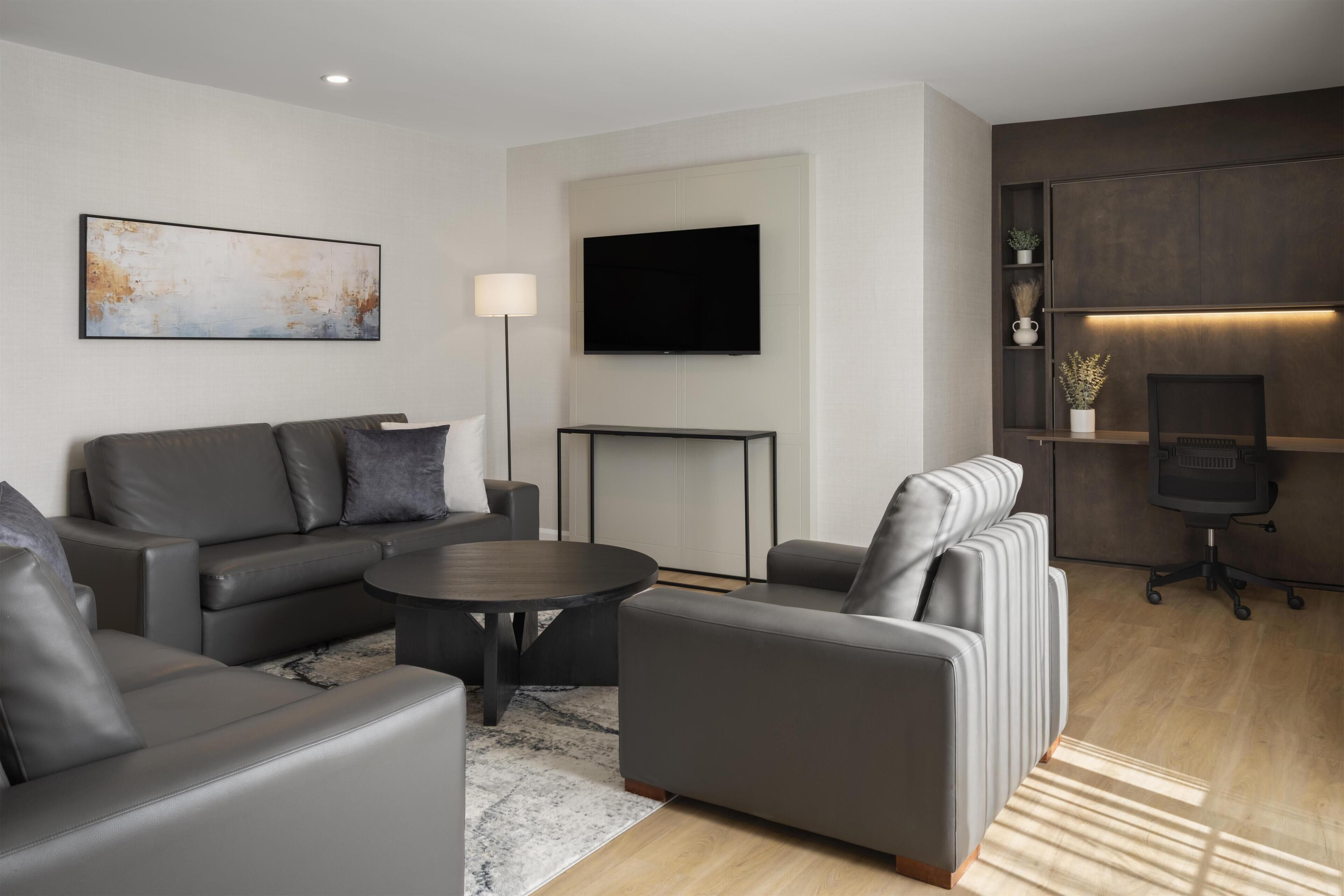 Uma sala de estar moderna com sofá, poltrona, mesa de centro, televisão de tela plana e uma mesinha de cabeceira com abajur.