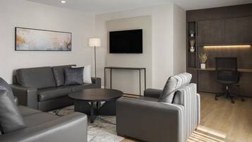 Uma sala de estar moderna com sofá, poltrona, mesa de centro, televisão de tela plana e uma mesinha de cabeceira com abajur.