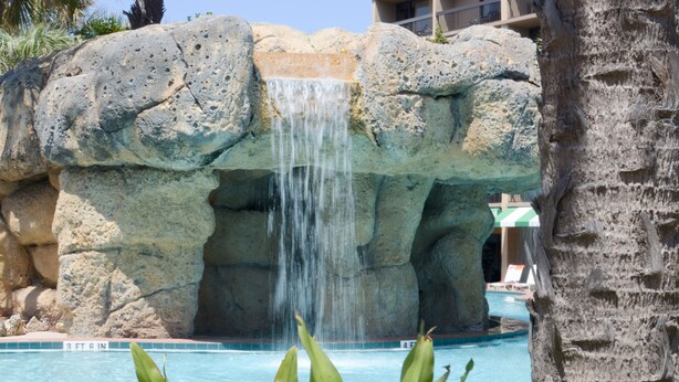 Piscina com cascata, cercada por grandes formações rochosas.