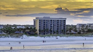 Um hotel na orla marítima com várias varandas, praia de areia e vista para o oceano.