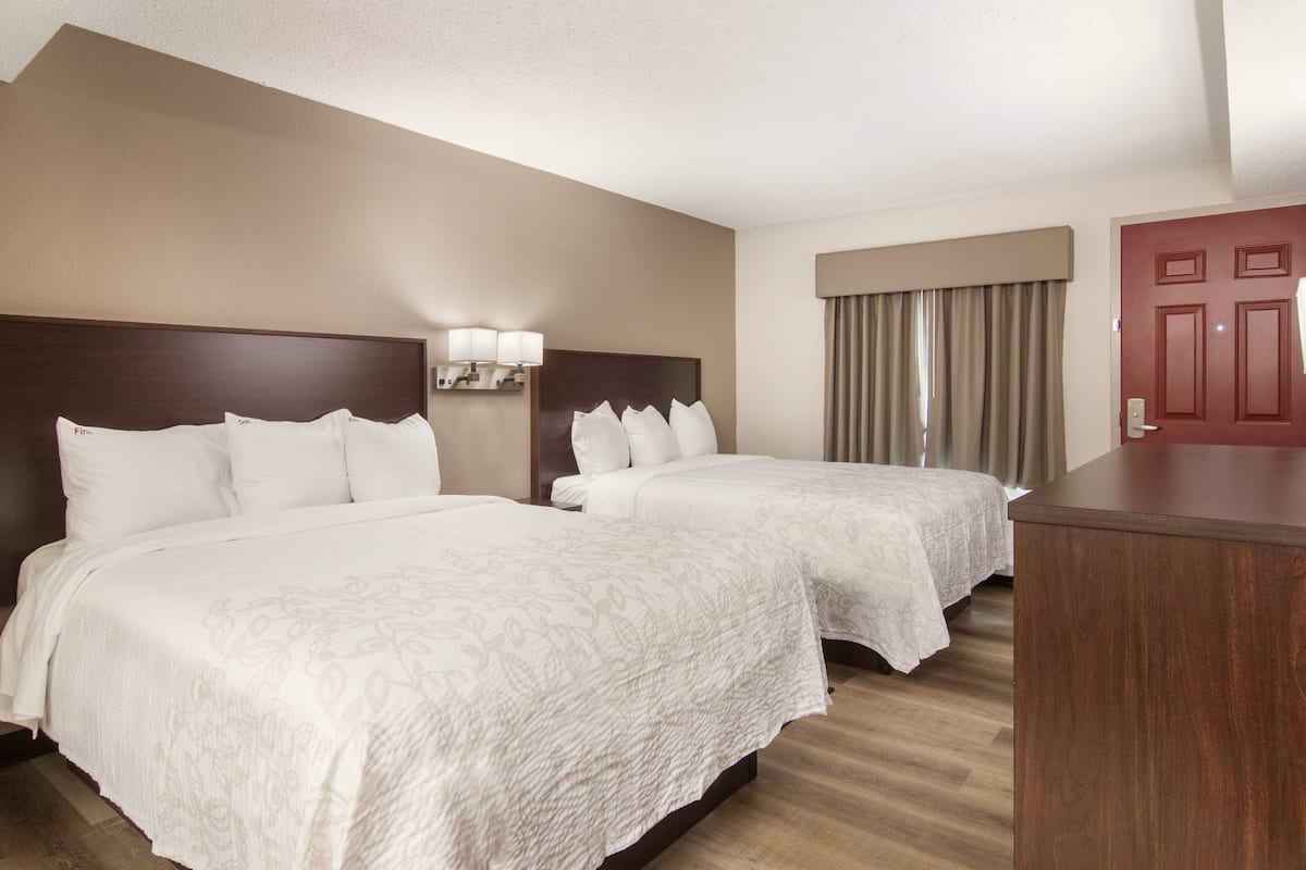 Quarto de hotel com duas camas, cabeceira de madeira, escrivaninha e janela com cortinas.