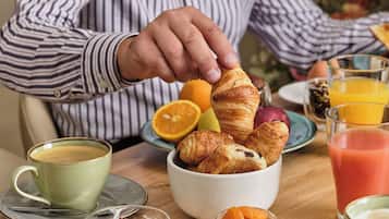 Uma pessoa vestindo camisa listrada esticando a mão para pegar um croissant de uma tigela.
