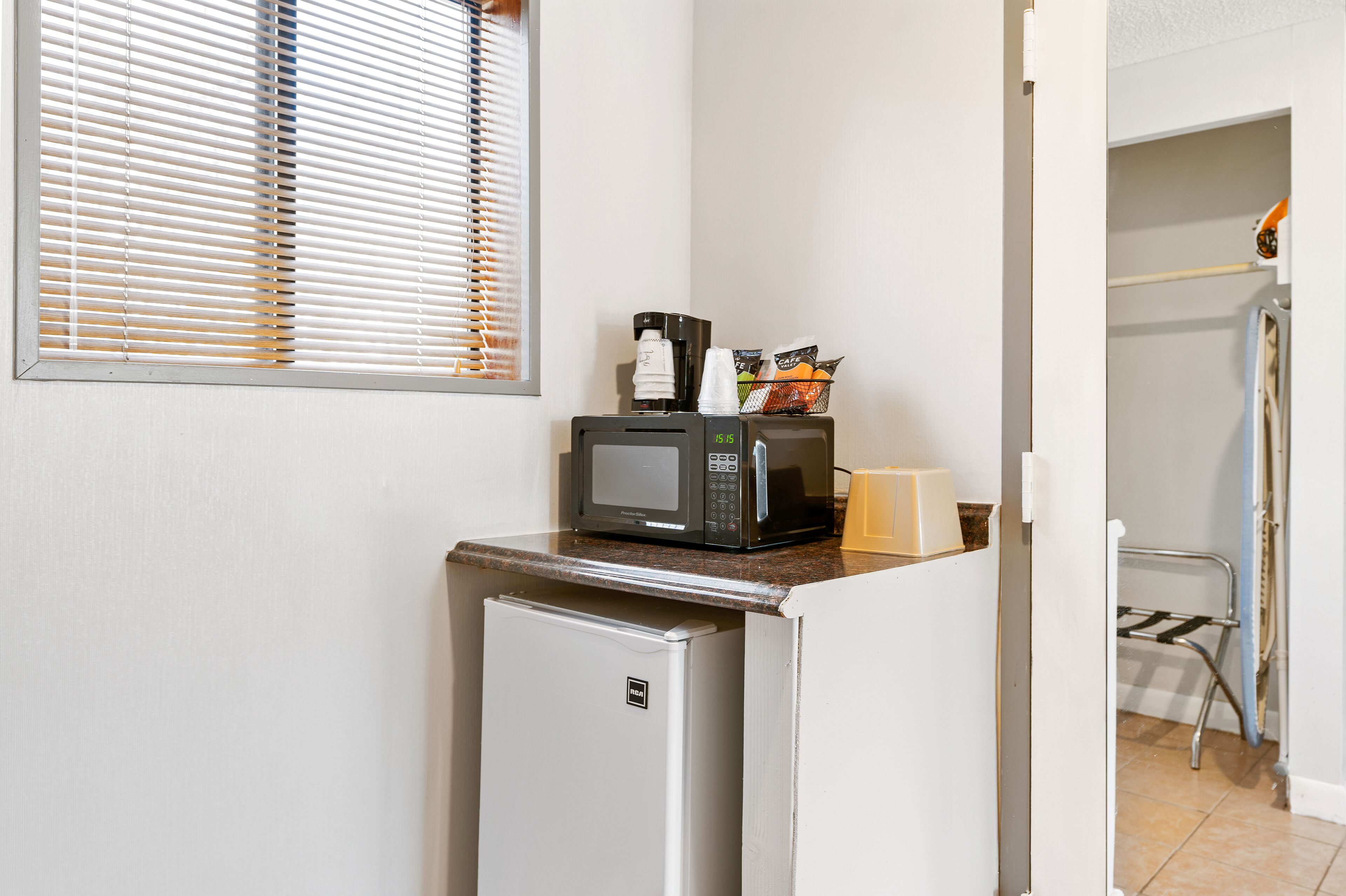 Uma cozinha compacta equipada com micro-ondas, máquina de café e um refrigerador pequeno.