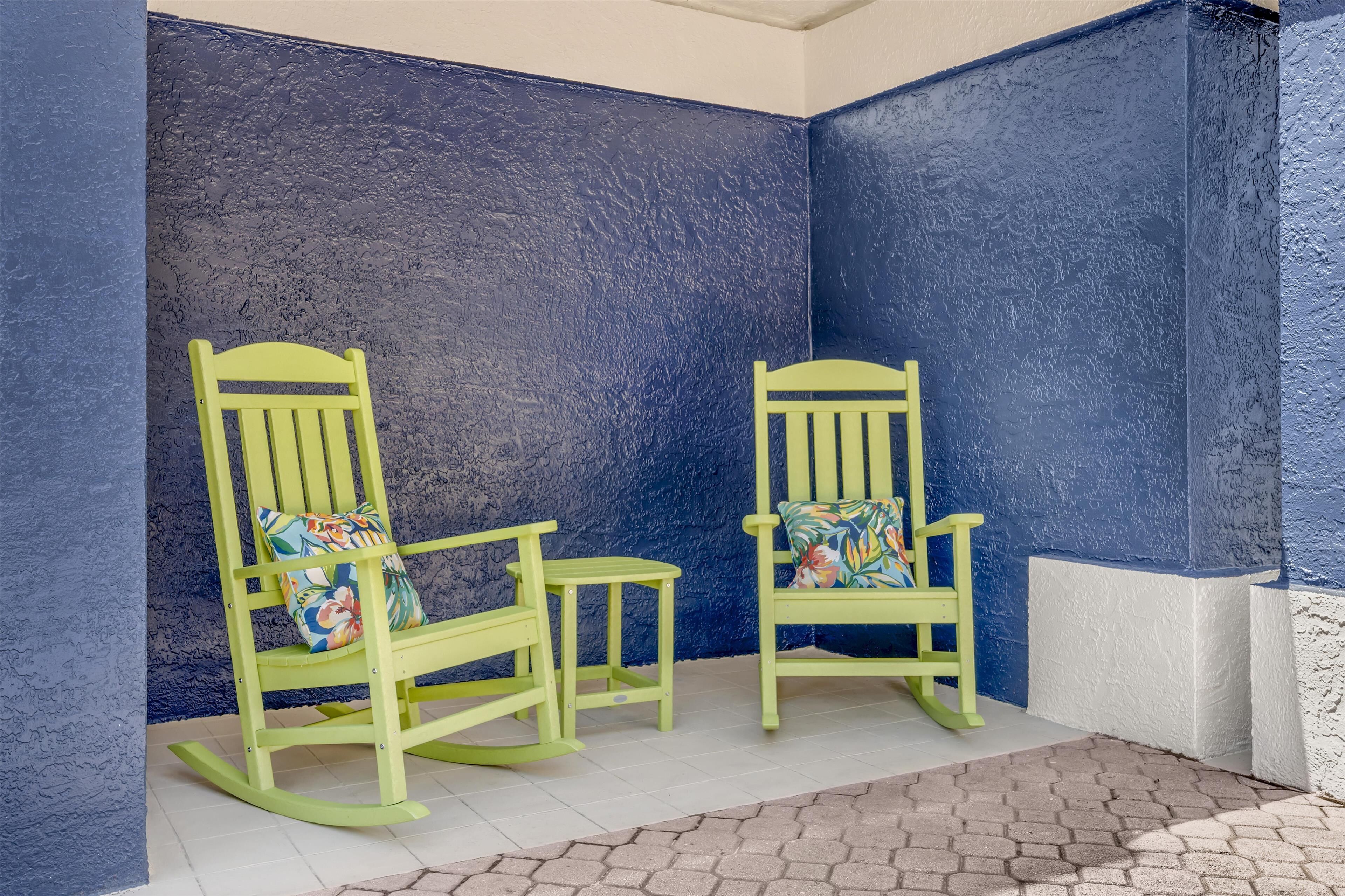 Canto com duas cadeiras de balanço e uma mesa pequena em frente a uma parede azul com textura.