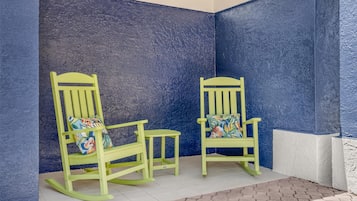 Canto com duas cadeiras de balanço e uma mesa pequena em frente a uma parede azul com textura.