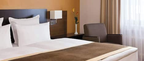 Quarto de hotel com uma cama grande, mesa de cabeceira com abajur, cadeira e vaso com flores.