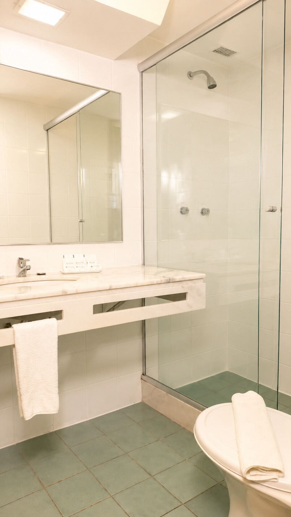 A bathroom with a glass-enclosed shower, a white sink with a mirror above it, and a toilet with a towel on it.