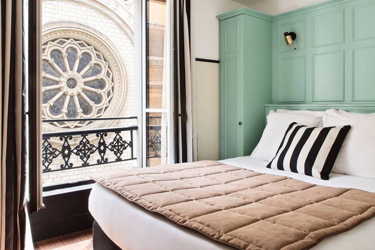 Quarto com uma cama grande, um guarda-roupa verde e uma janela com vista decorativa.