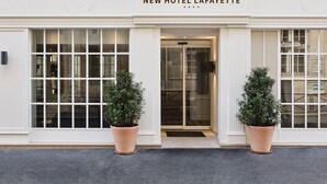Fachada do Hotel Lafayette, com grandes janelas, entrada central e dois vasos de plantas de cada lado.