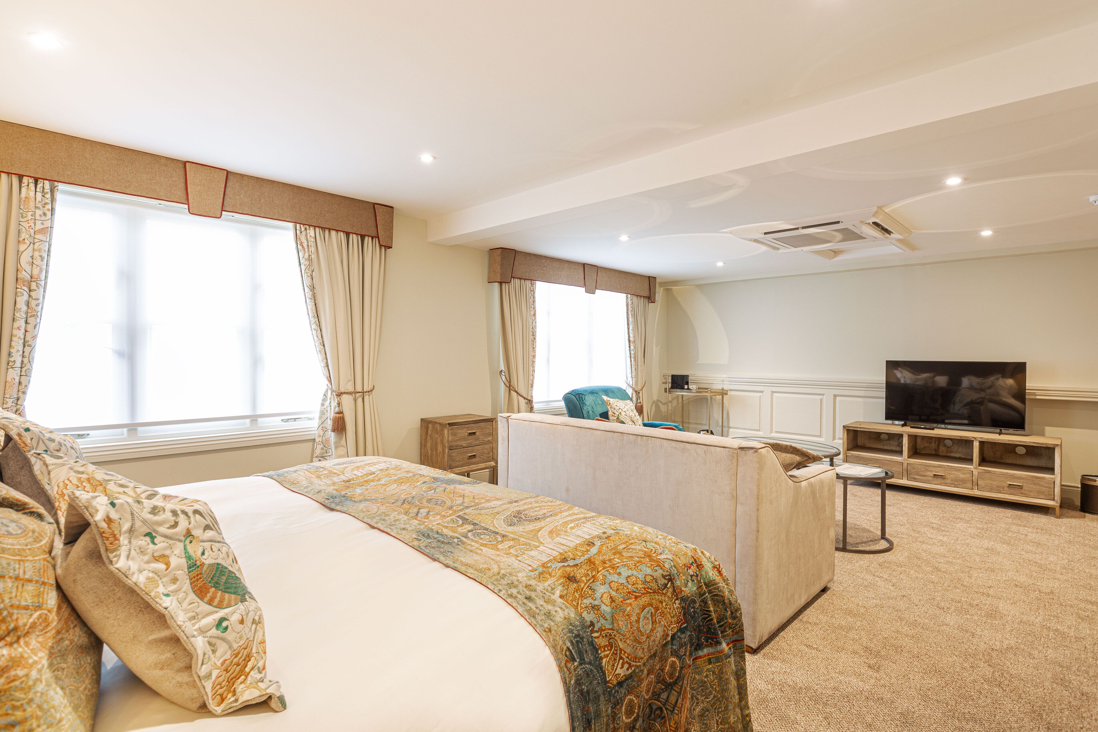 Quarto de hotel com uma cama grande, uma escrivaninha, uma televisão e uma janela com cortinas.