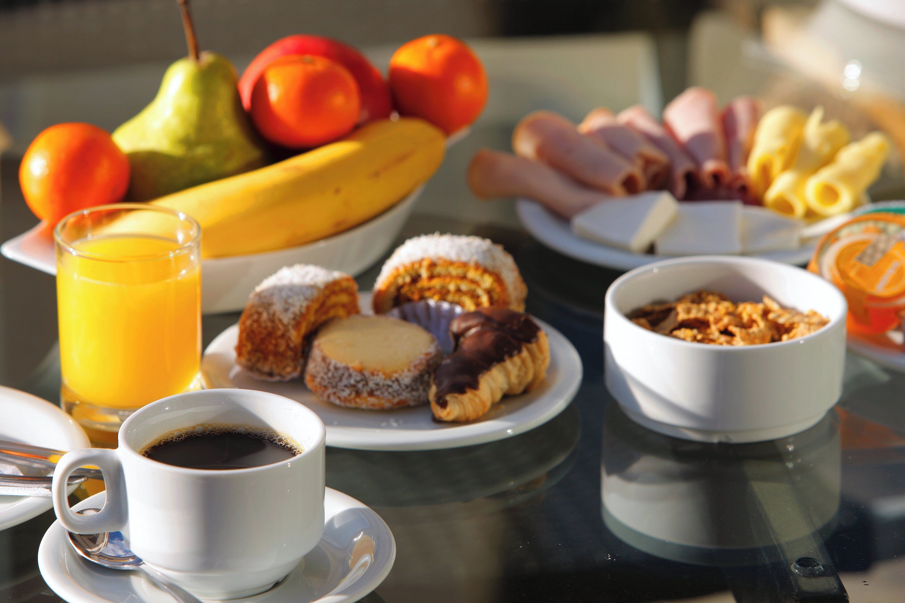 Uma mesa de café da manhã com diversos alimentos, incluindo frutas, doces e uma xícara de café.