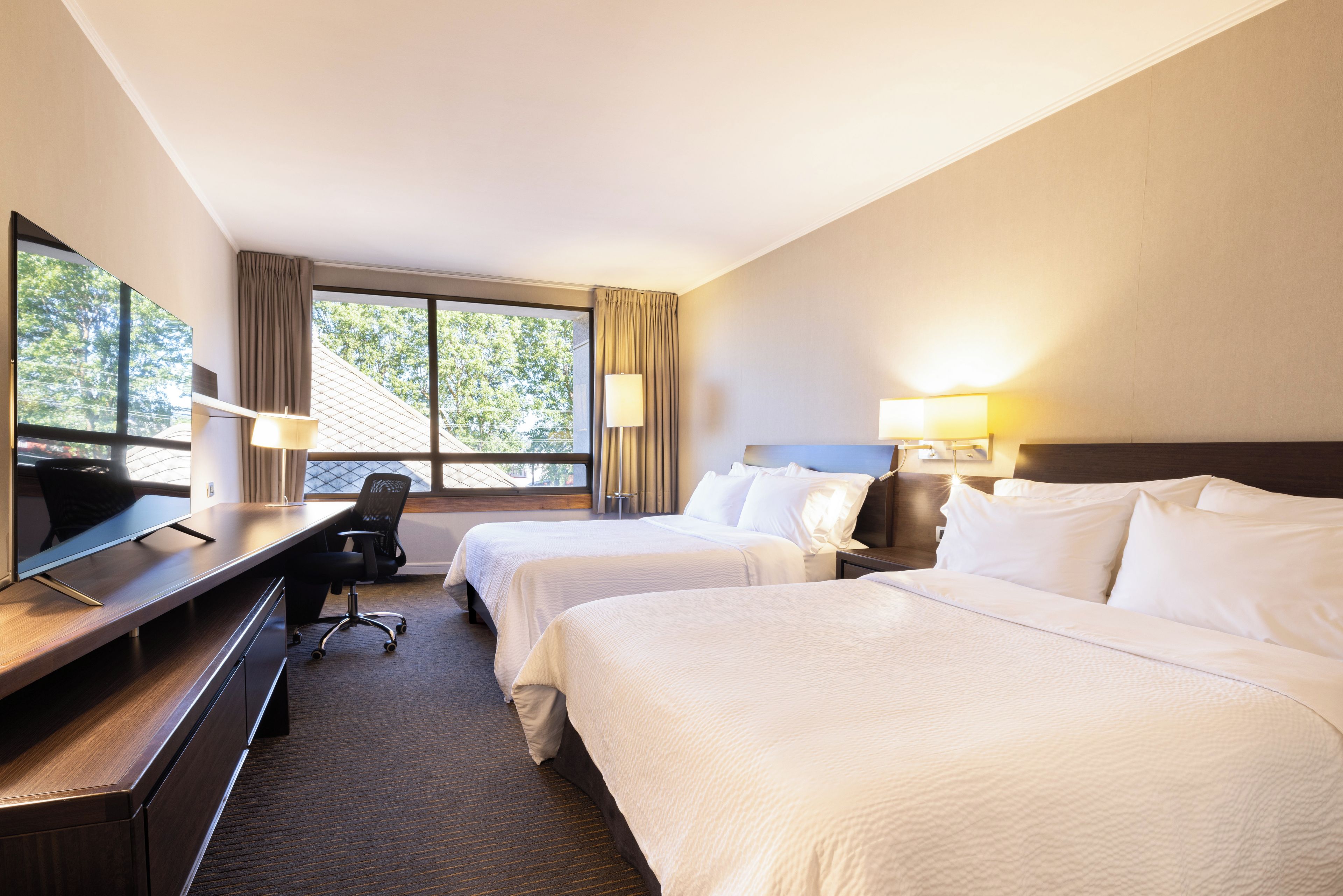 Quarto de hotel com duas camas, uma escrivaninha, uma cadeira e uma televisão.