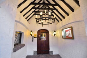 Um corredor com porta de madeira, paredes brancas e um candelabro.