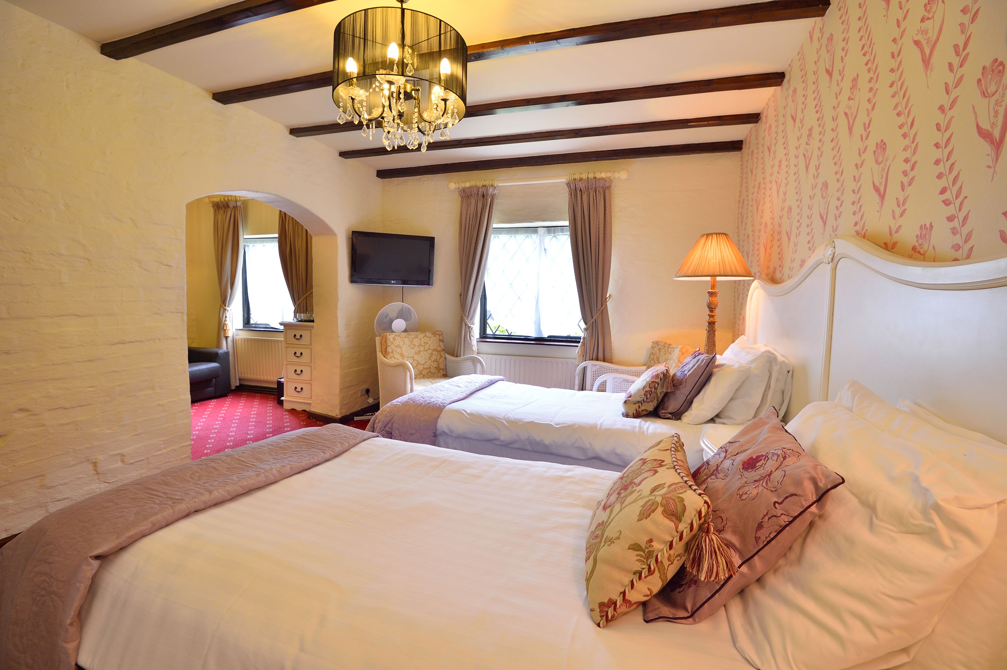 Quarto de hotel com duas camas, televisão, um candelabro e janela com cortinas.