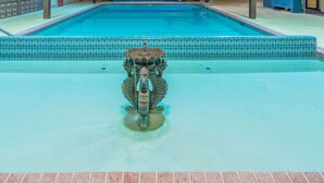 Piscina com uma fonte decorativa no centro, borda azulejada e um deck de tijolos com uma placa indicando a profundidade.