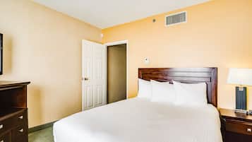 Quarto de hotel com uma cama grande, cômoda, mesa de cabeceira e luminária.