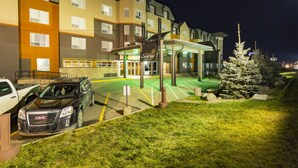 Um hotel com vários andares, entrada central, área de estacionamento e um pinheiro de Natal.