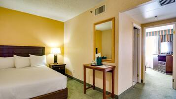 Quarto de hotel com cama grande, mesa de cabeceira, espelho e escrivaninha com cadeira.