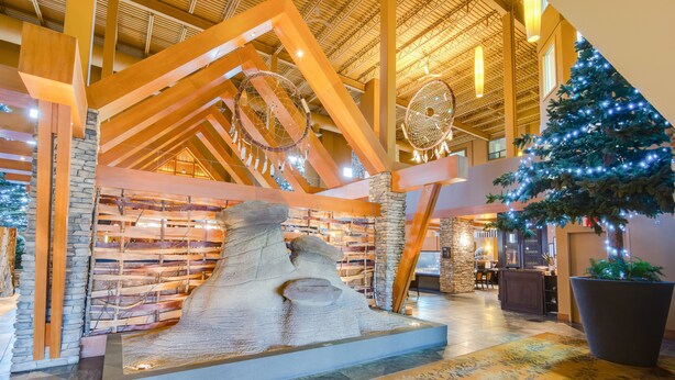Um hall espaçoso com uma grande escultura de pedra, vigas de madeira e um pinheiro de Natal.