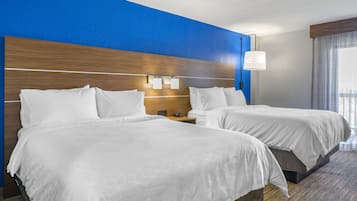 Quarto de hotel com duas camas, cabeceira de madeira, parede azul decorativa e mesa de cabeceira com abajur.