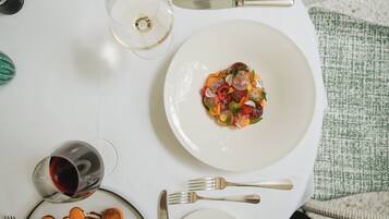 Uma mesa de jantar com um prato de comida, um copo de vinho tinto e talheres.
