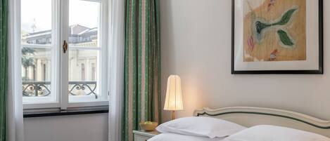Quarto de hotel com cama, mesa de cabeceira com abajur, quadro na parede e janela com cortinas.